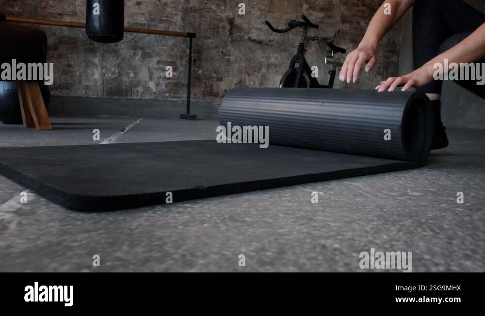 Fit woman rolls out black mat on floor in gym near laptop Stock Video ...