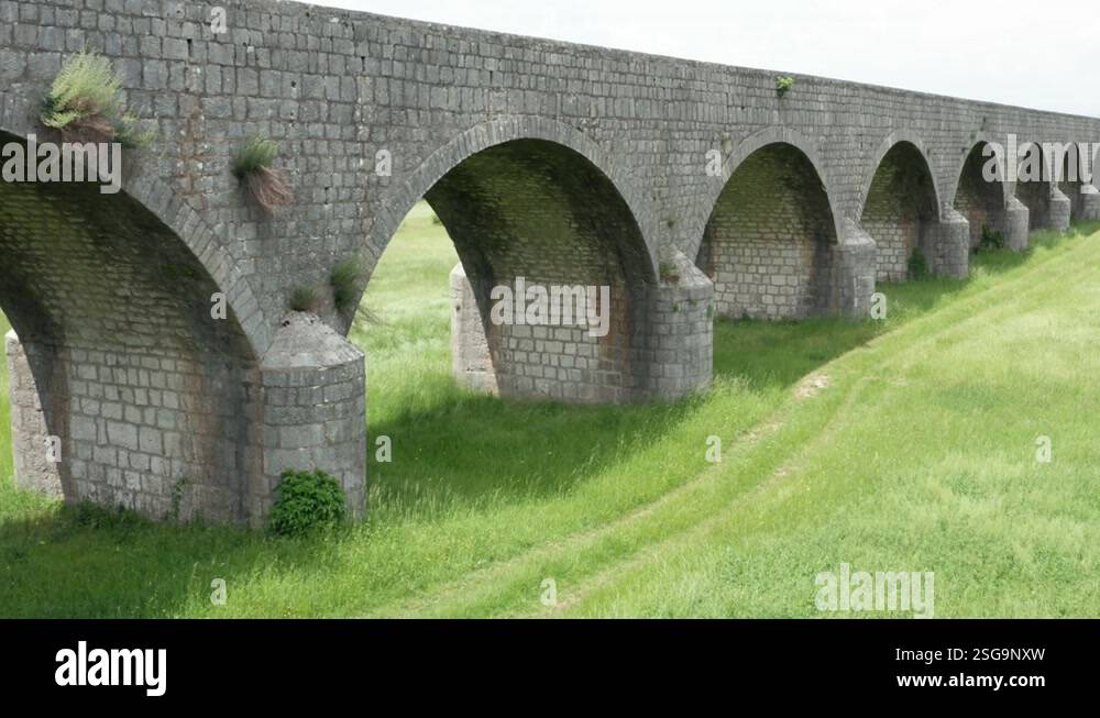 Old arch bridge made of stone over a green grassy field - long vintage ...