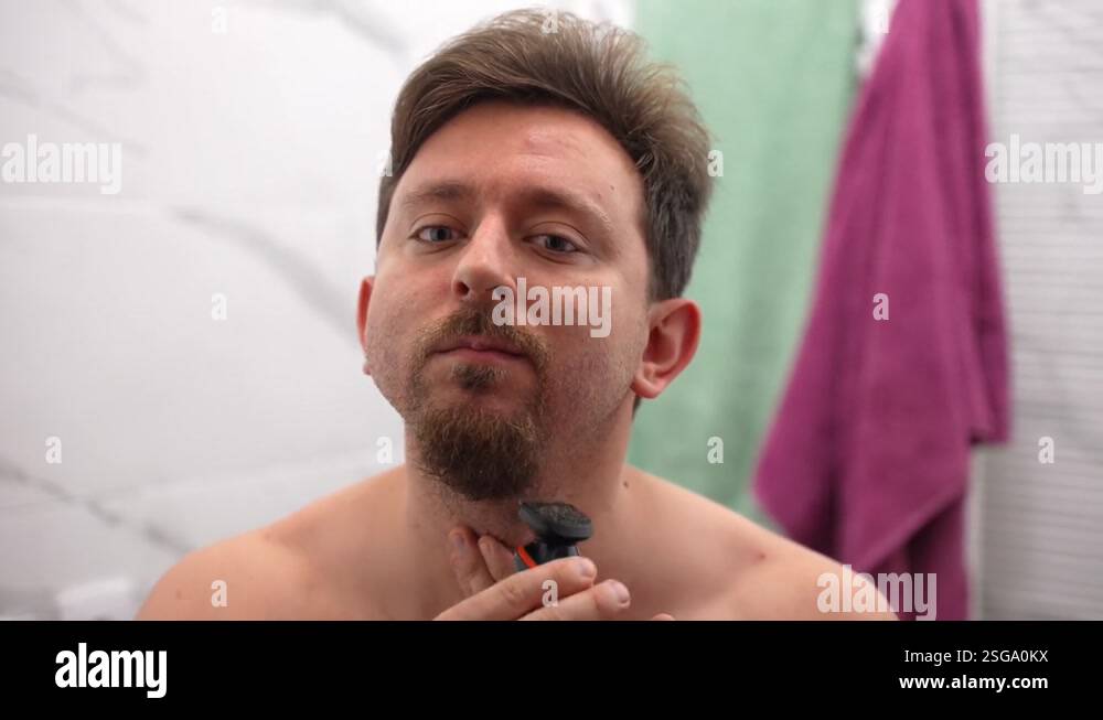 Attractive young man shaving cheeks, moustache and beard with electric ...