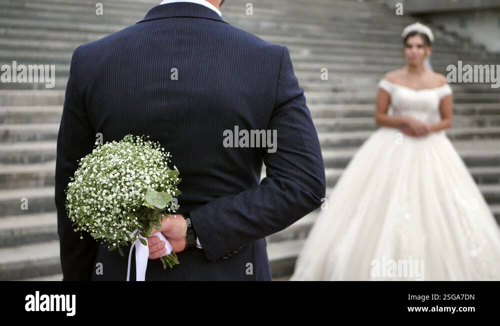 the groom hides the wedding bouquet of flowers behind his back in the ...