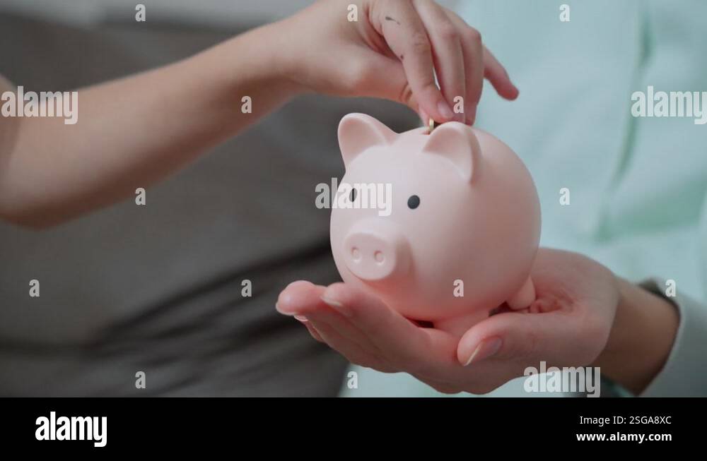 Children's hands alternately drop coins into a pink piggy bank Stock ...