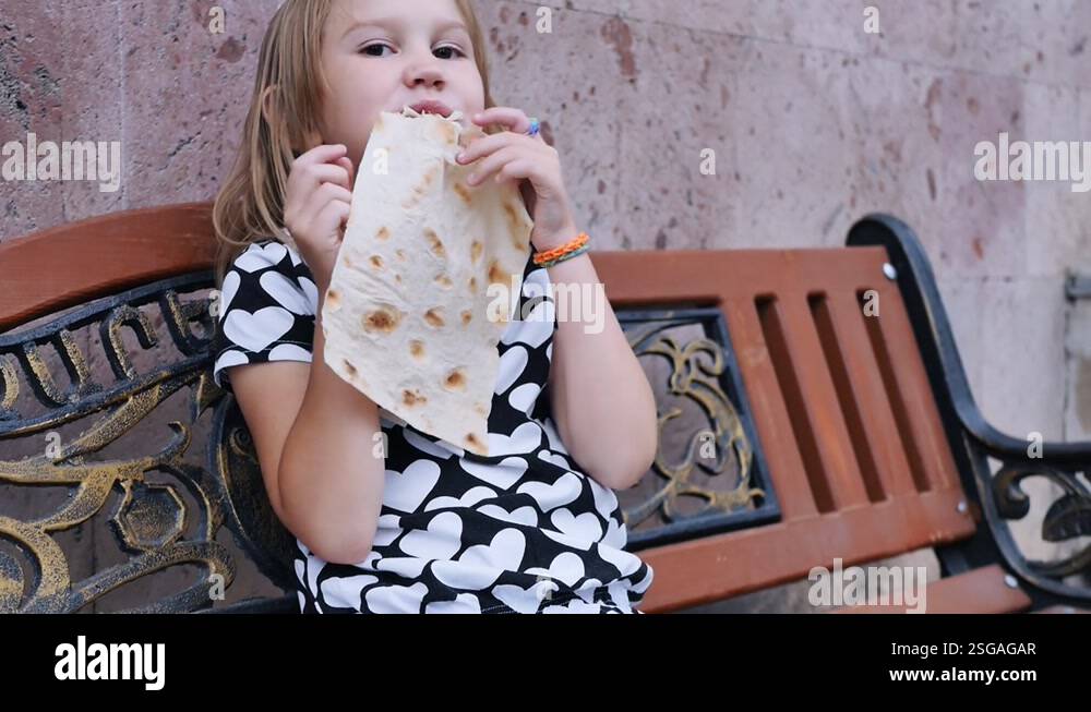 A cute and pretty teenager girl eats a baked pita holding in her hands ...
