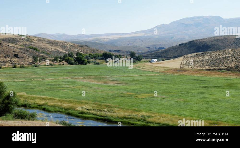 Homestead in the distance across a grassy meadow in the hills of ...