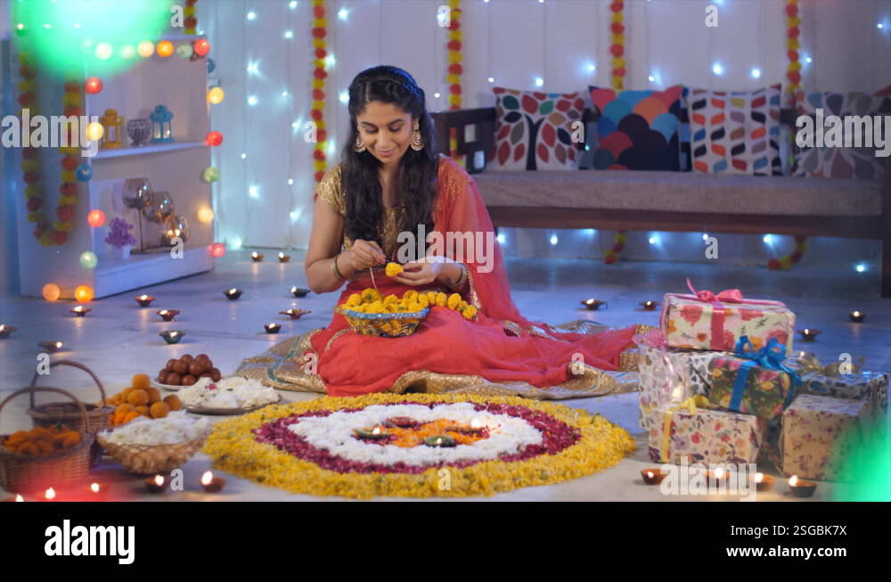A young Indian lady is preparing flower garlands (Mala) for Diwali Puja ...
