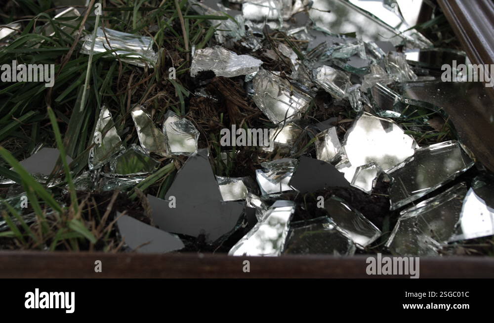 A broken and shattered mirror lays on the ground with reflective shards ...