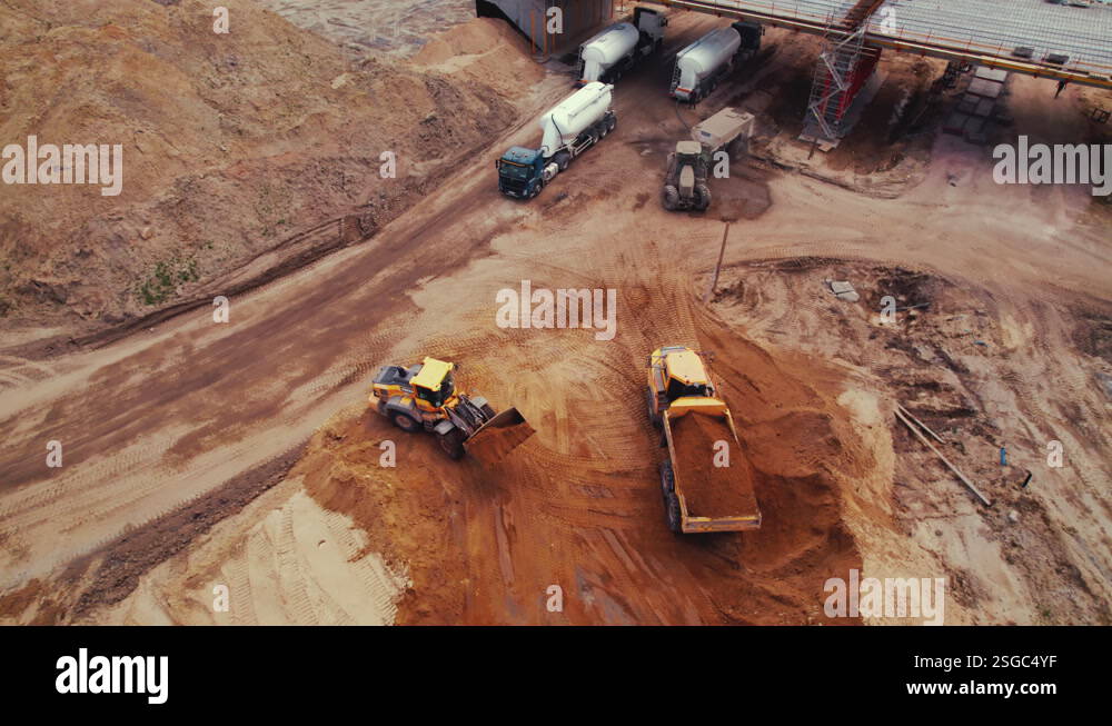 A bulldozer with a blade full of earth loading an industrial dumper ...