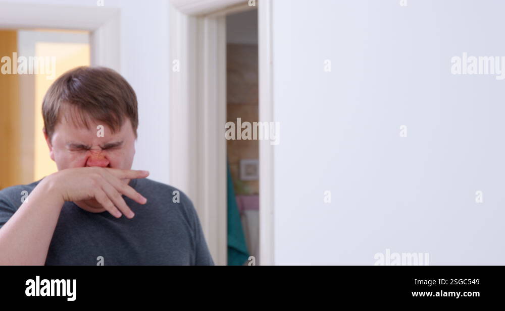 Sick man comes into room and sneezes hard, covering mouth with hand ...