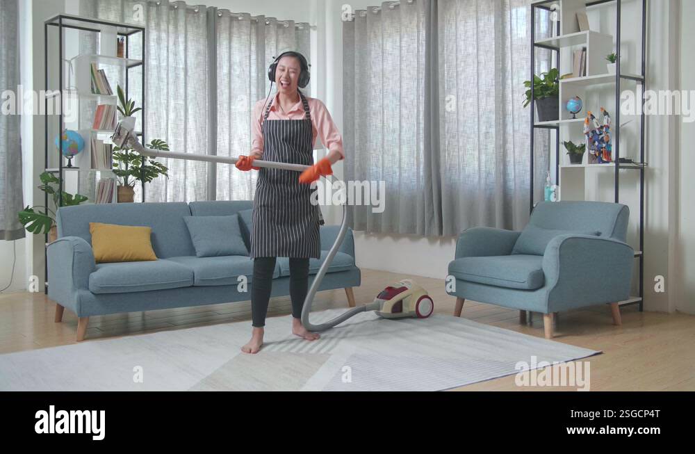 Asian Female Housekeeper With An Apron Wearing Headphones, Listening To ...