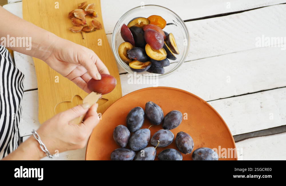 Top view woman's hands cut fresh plums into pieces with a knife ...