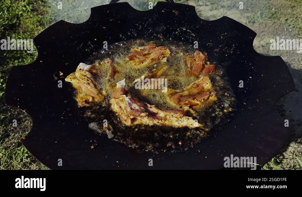 A man's hand puts meat in boiling oil in a brazier on an open fire ...