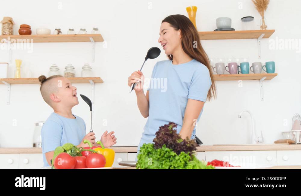 Happy little boy DJing in the kitchen, mother and son singing a song ...
