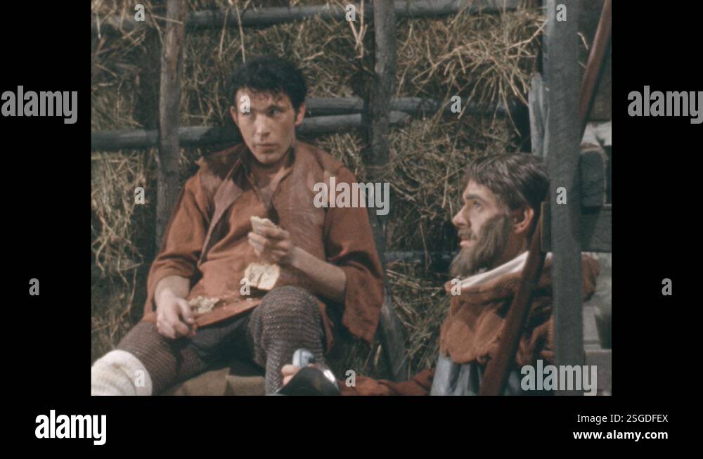 1940s: Men in medieval peasant clothing sit in stable. Man holds loaf ...