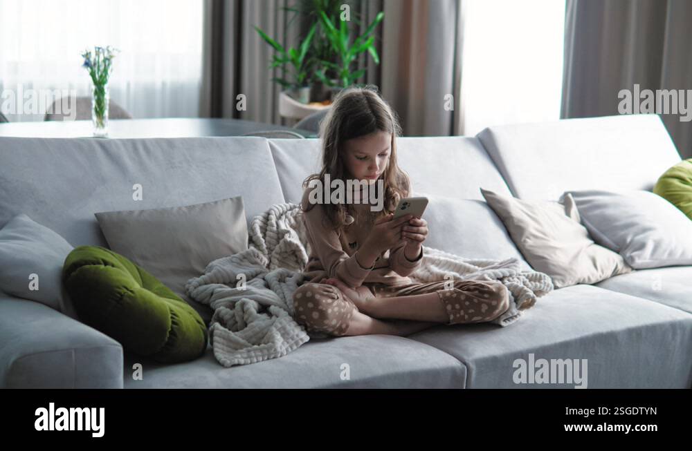 Cute sweet child girl in pajamas just woke up and now using mobile ...