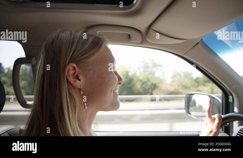 happy young woman driving car along highway ahead and smiles. blonde ...