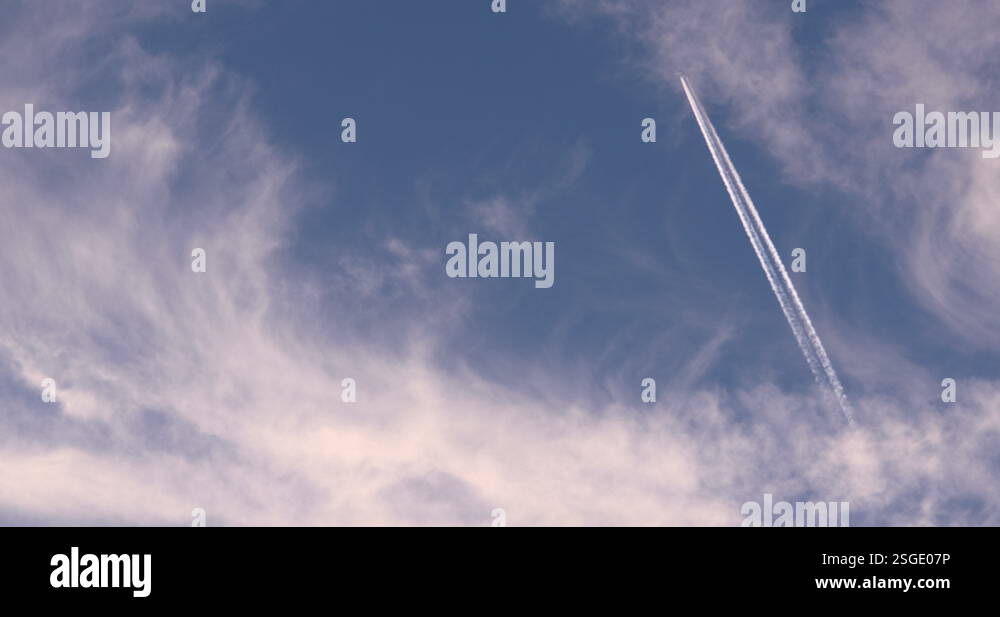 Jet airplane flying across blue sky trailing vapour contrail stream ...