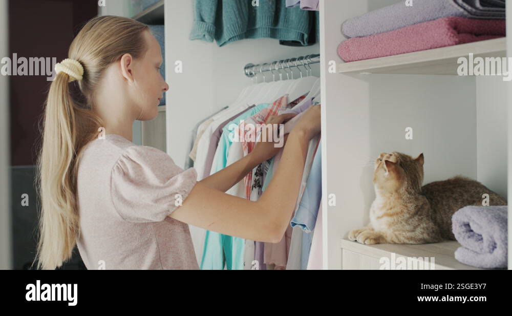 A child chooses an outfit in her dressing room, her cat sits next to ...