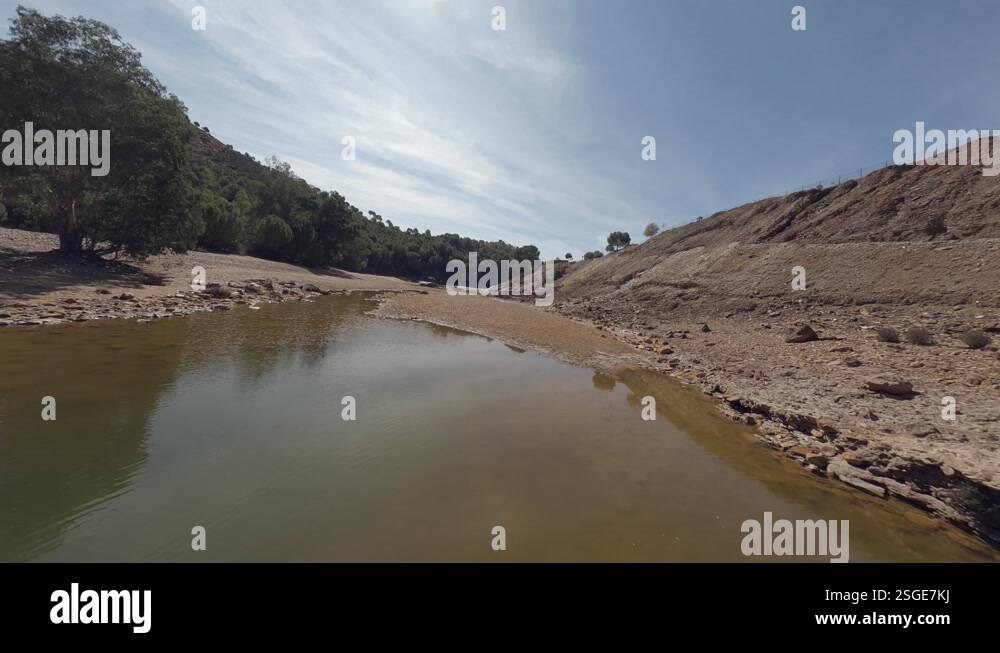 Low fast FPV aerial along dry rocky Odiel River bed to old arch bridge ...