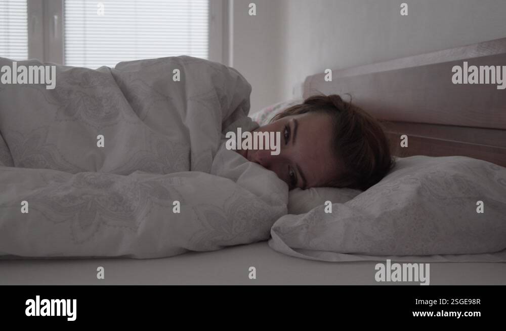 Sleeping girl opening eyes, waking up in morning, tired face, closeup ...