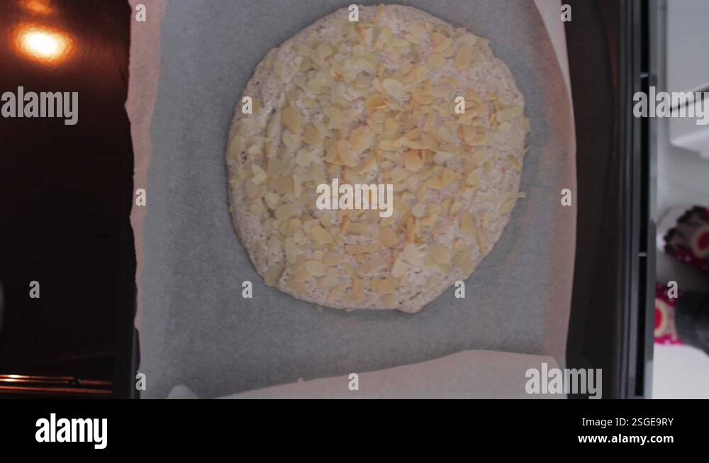 A woman baker puts a baking sheet with cream and almond flakes in the ...