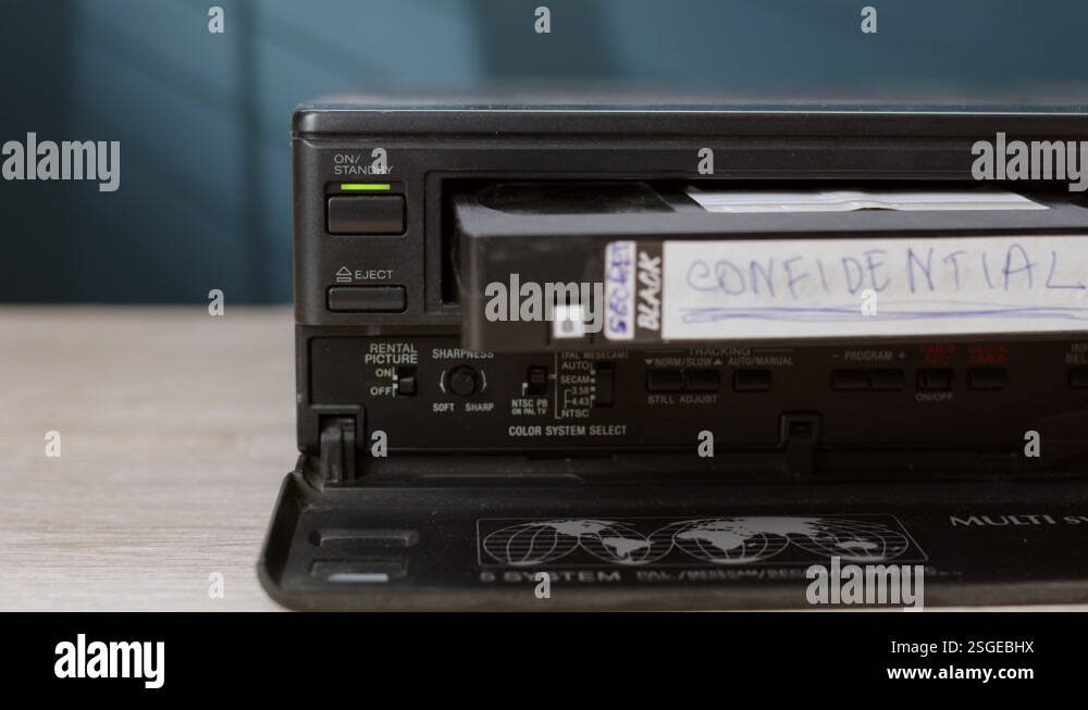 man inserts old black cassette tape into VHS player labeled ...