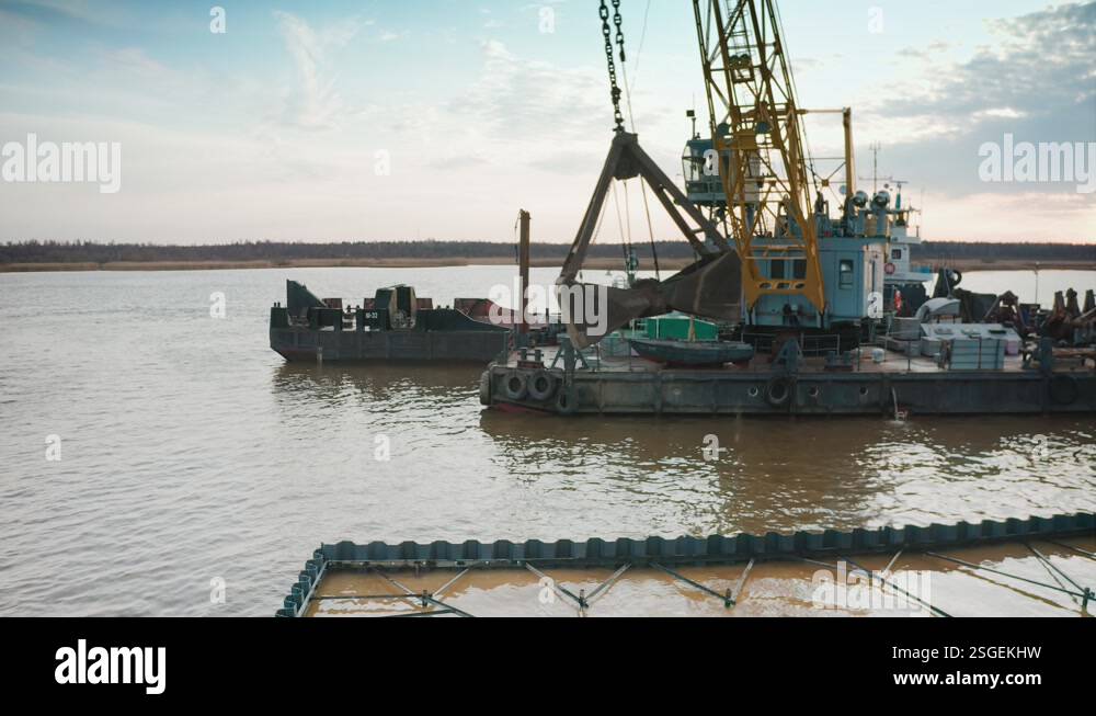 A crane bucket unloading sand from a barge to strengthen the shore by ...