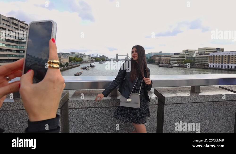 Pretty young woman poses on London Bridge while a woman takes a picture ...