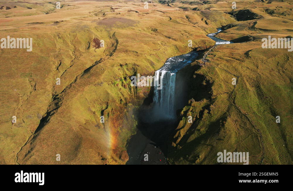 Wide aerial pan down over small group of tourists admiring Skogafoss ...