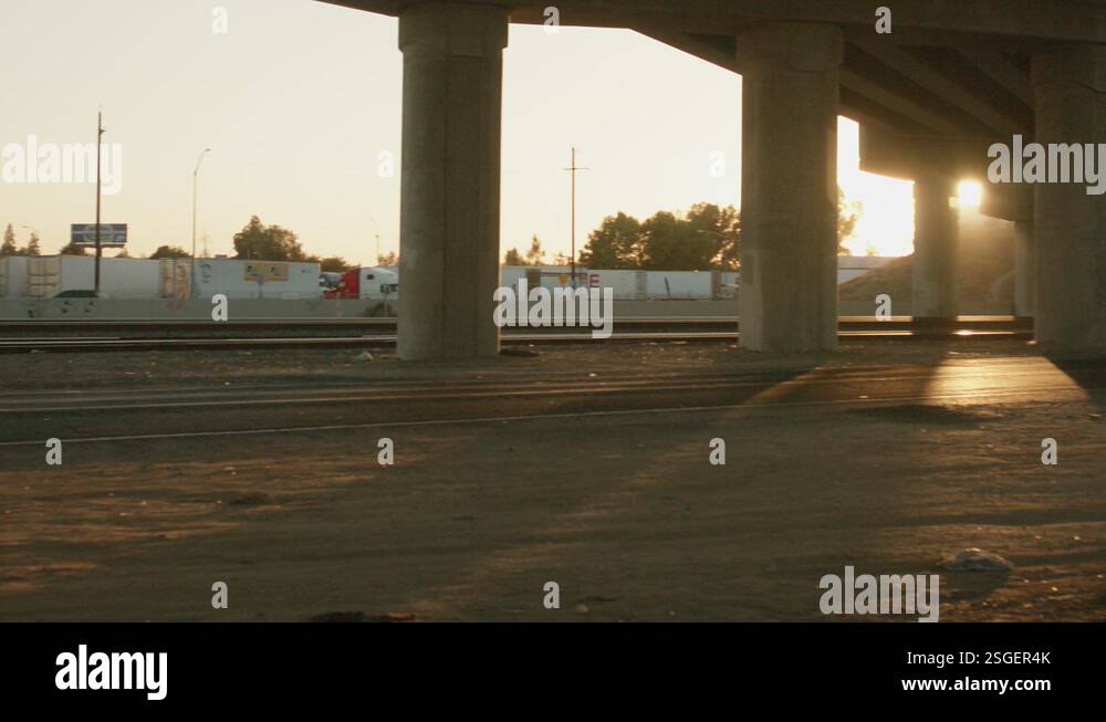 Cargo train pass under freeway bridge though traffic during sunset ...