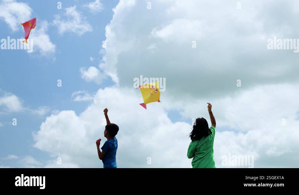 silhouette shot, back view of two preteen kids flying kite on blue ...