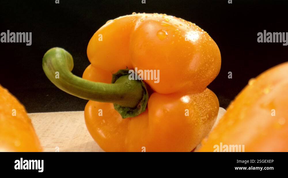 Close up shot of ripe fresh yellow peppers on wooden board. Drops of ...