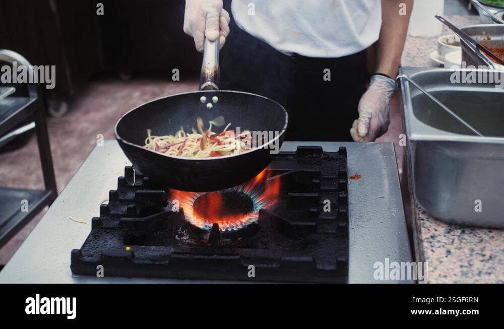 Flying asian noodles with vegetable from pan. Chef preparing flambe ...