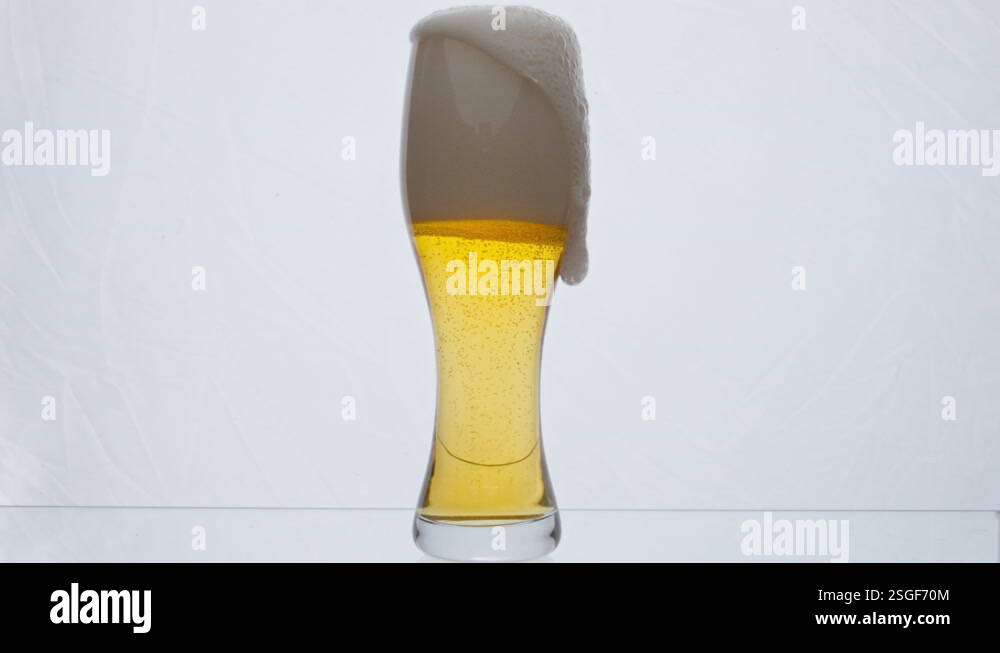 Glass full foamy beer overflowing in super slow motion close up ...