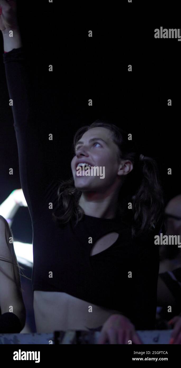 Girl dancing in crowd in front of stage with flashing lights. Vertical ...