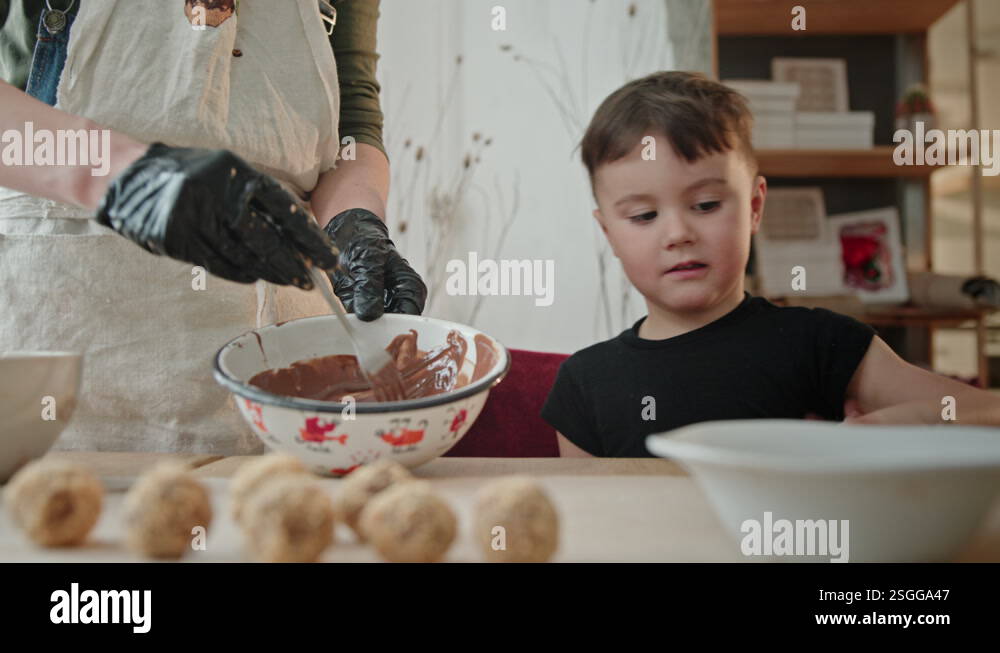 Mother and son making cookies together. Child putting cookie into bowl ...