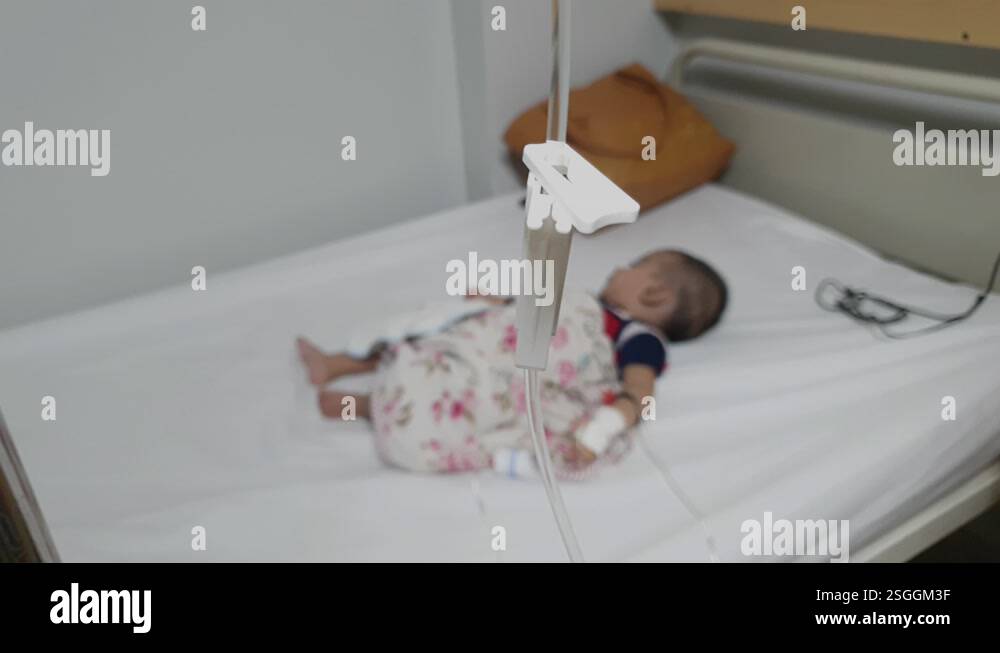 Foreground Focus On IV Drip Attached To Sick Baby In Hospital Bed In ...