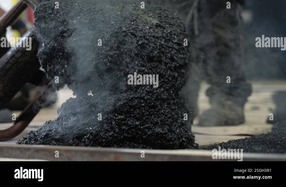 Worker dumping the tar from the wheelbarrow on the surface where he is ...