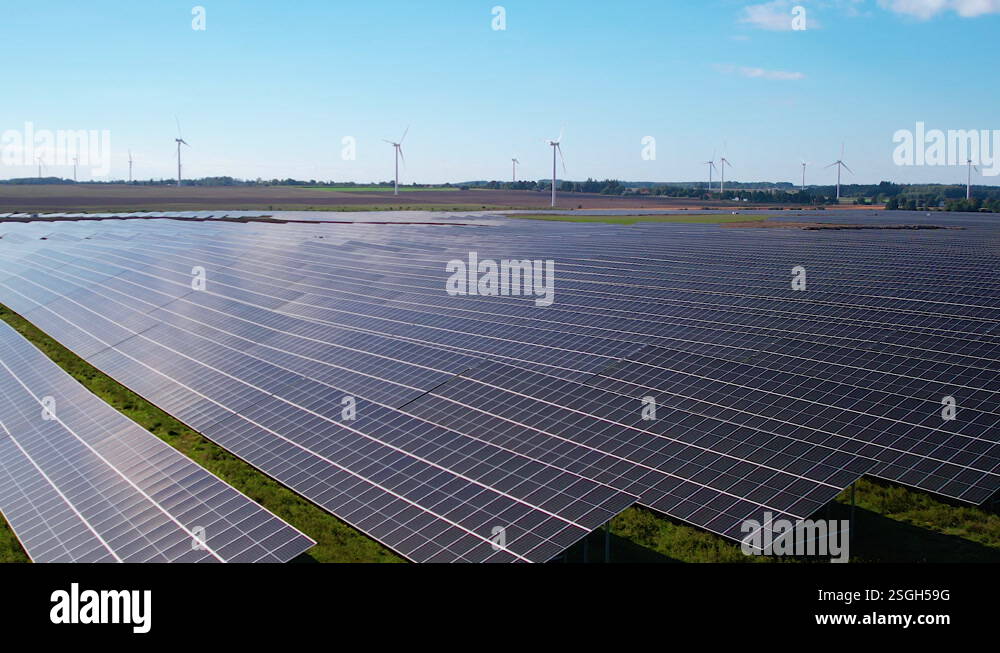 Slow Dolly Left View Of Large Scale Solar Panel Farm With Windmills In ...