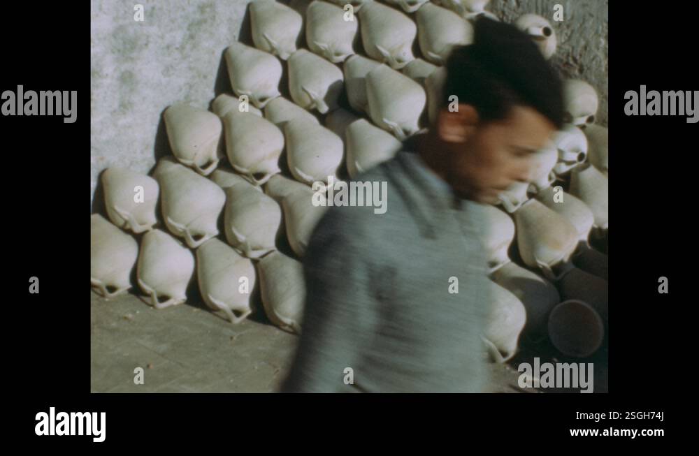1950s:Man picks up jug from a pile of jugs on the ground and carries it ...