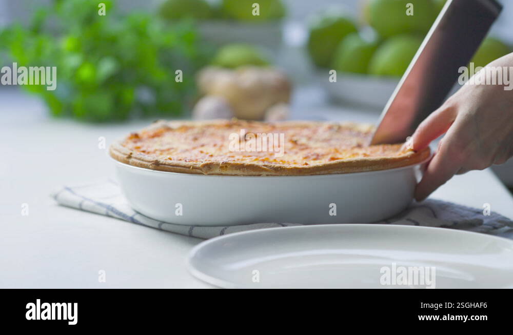 woman in the kitchen cutting a pie with potatoes, cheese and sausages ...