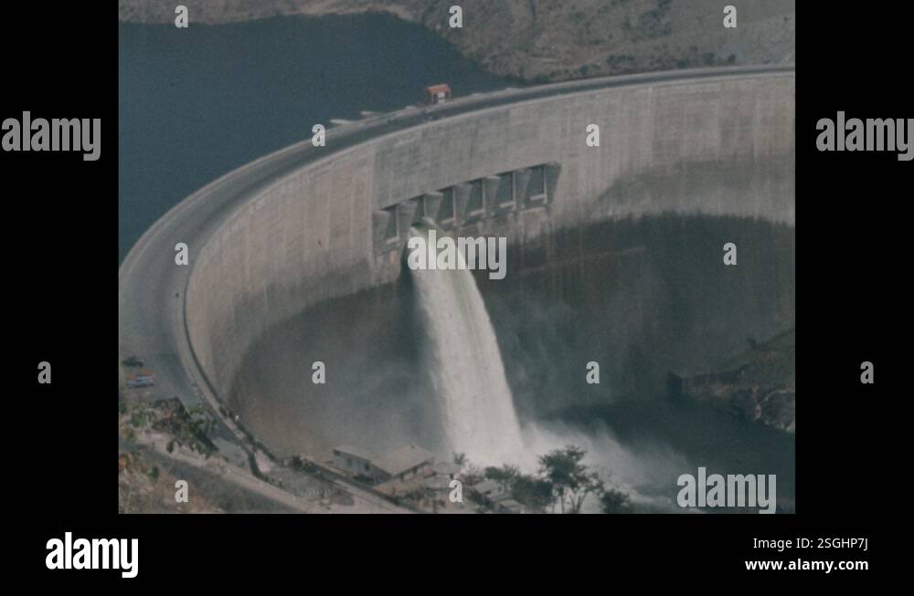 1950s: Water pours from hydroelectric dam. Cars drive across large man ...