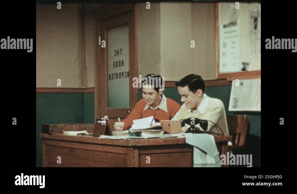 1940s: Two teen boys sit at drafting table, look at papers, talk, write ...