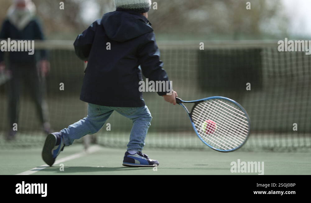 Back of kid playing tennis with parent during winter season. Child ...