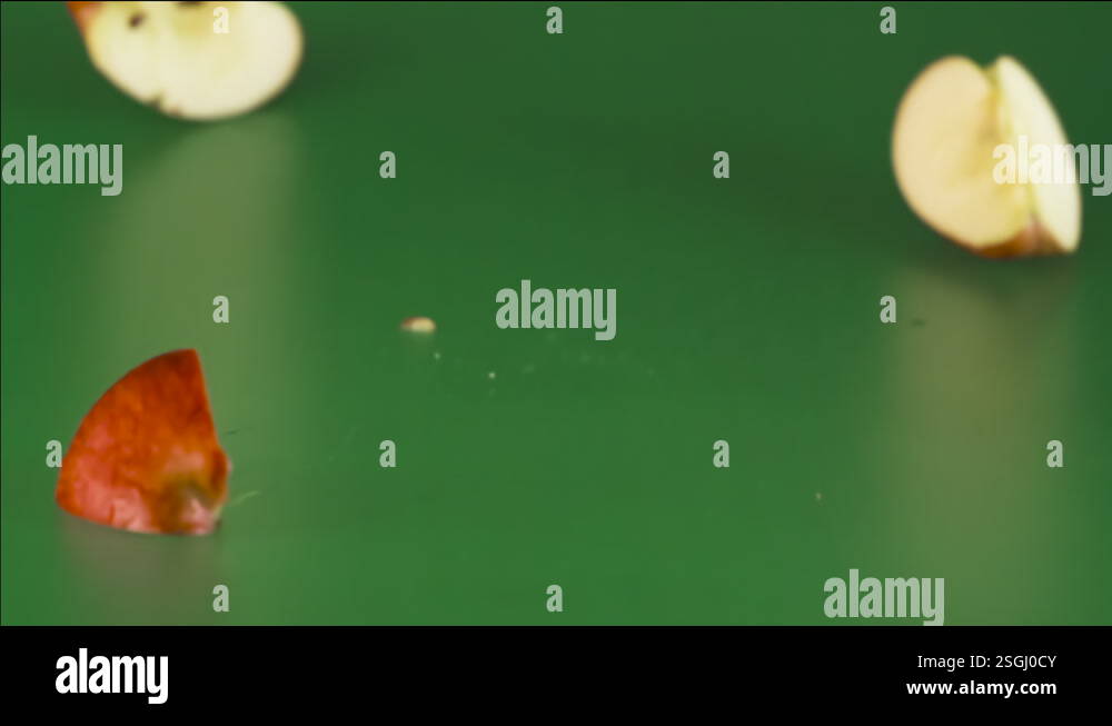 Red apple falling and breaking into a lot of pieces on a green ...