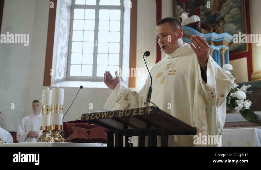 Priest in white robe stands near pulpit during Sunday Mass and begins ...
