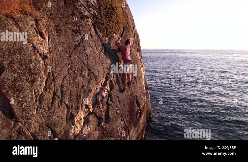 Male rock climber over the ocean, free solo, no rope, adventure sport ...