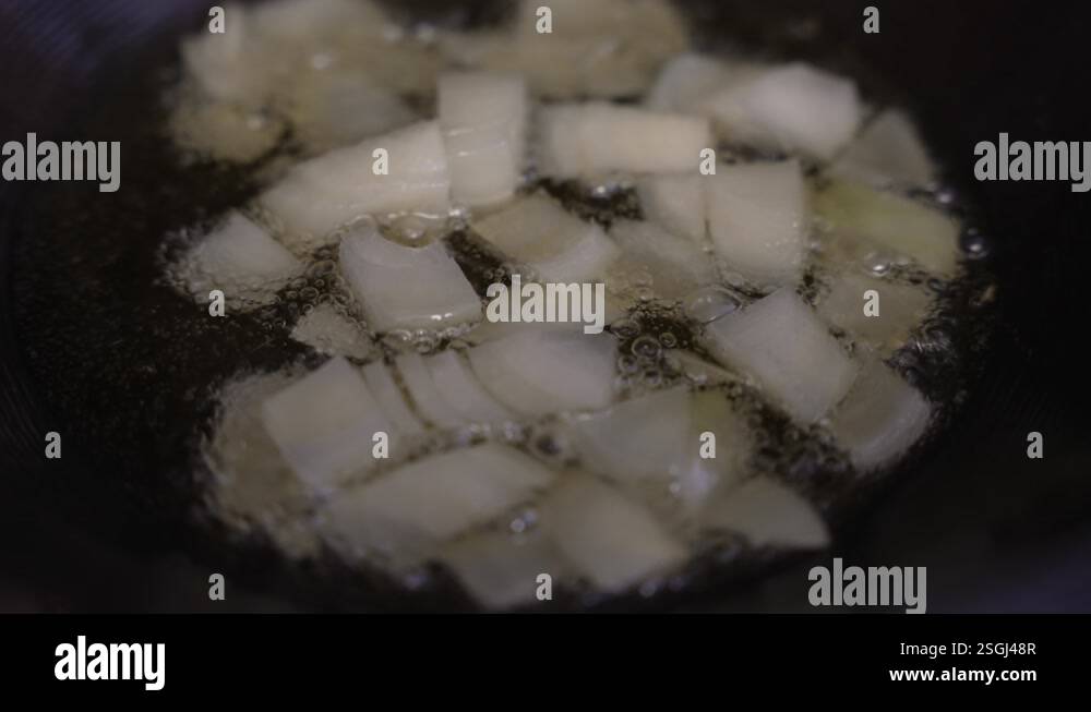 A close up shot of raw diced onions sizzling inside hot carbon steel ...