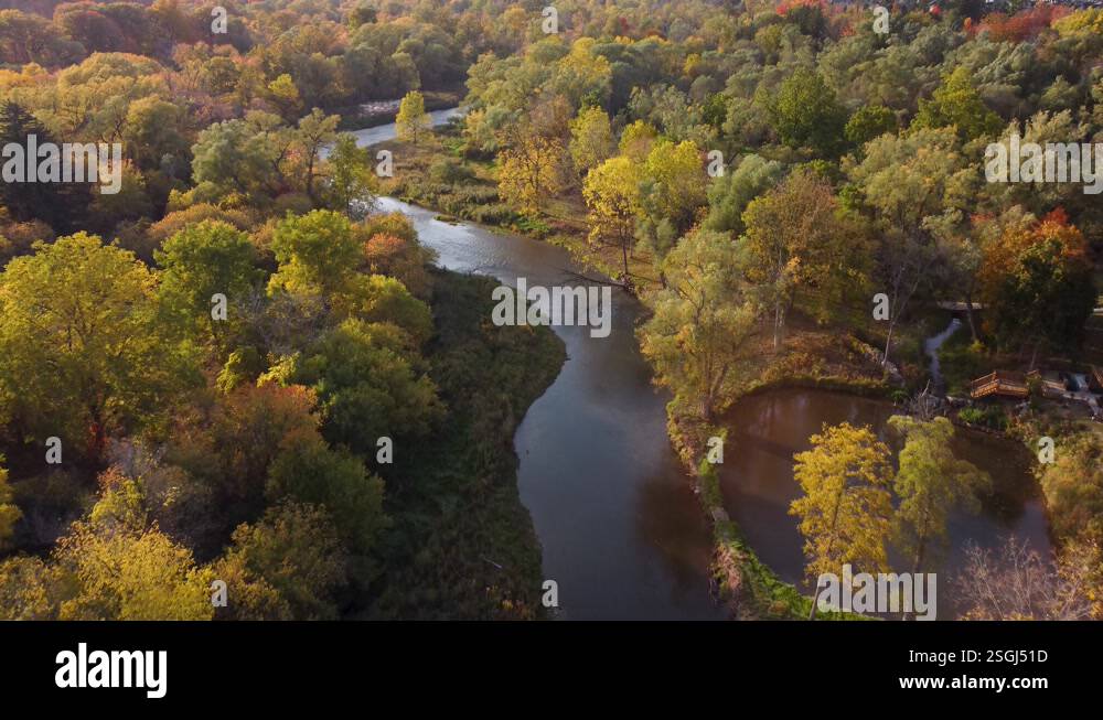 Fly over park and trees in warm red and orange colors. A calm river in ...