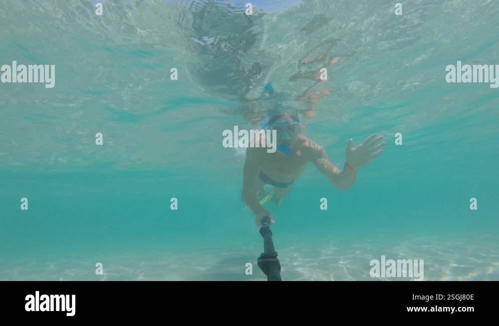 A friendly Caucasian young man in an underwater mask and fins waves his ...