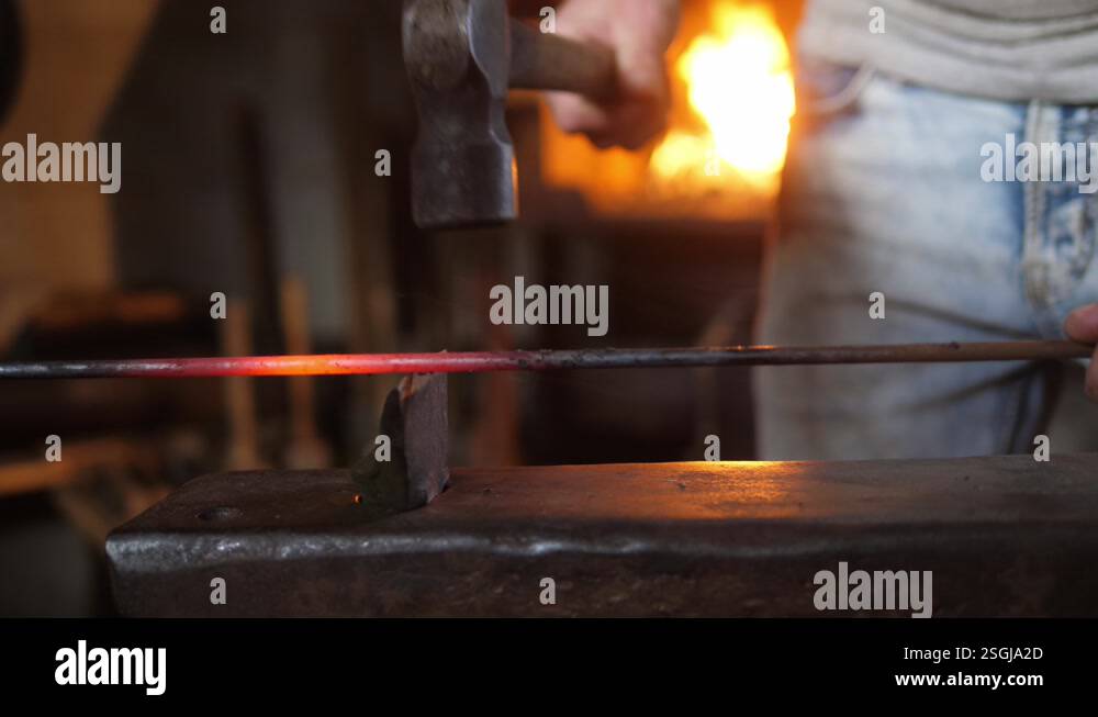 Blacksmith striking and breaking red hot metal rod with hammer on anvil ...