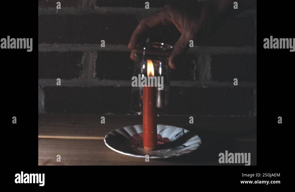 1950s: hand places glass over lit candle. Red candle and flame ...